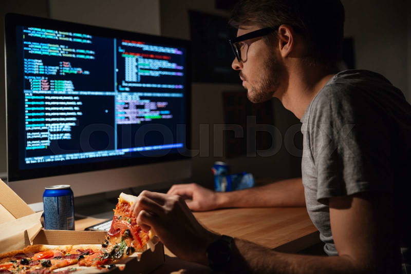 Profile of concentrated young software developer eating pizz | Colourbox Profile of concentrated young software developer eating pizz | Colourbox