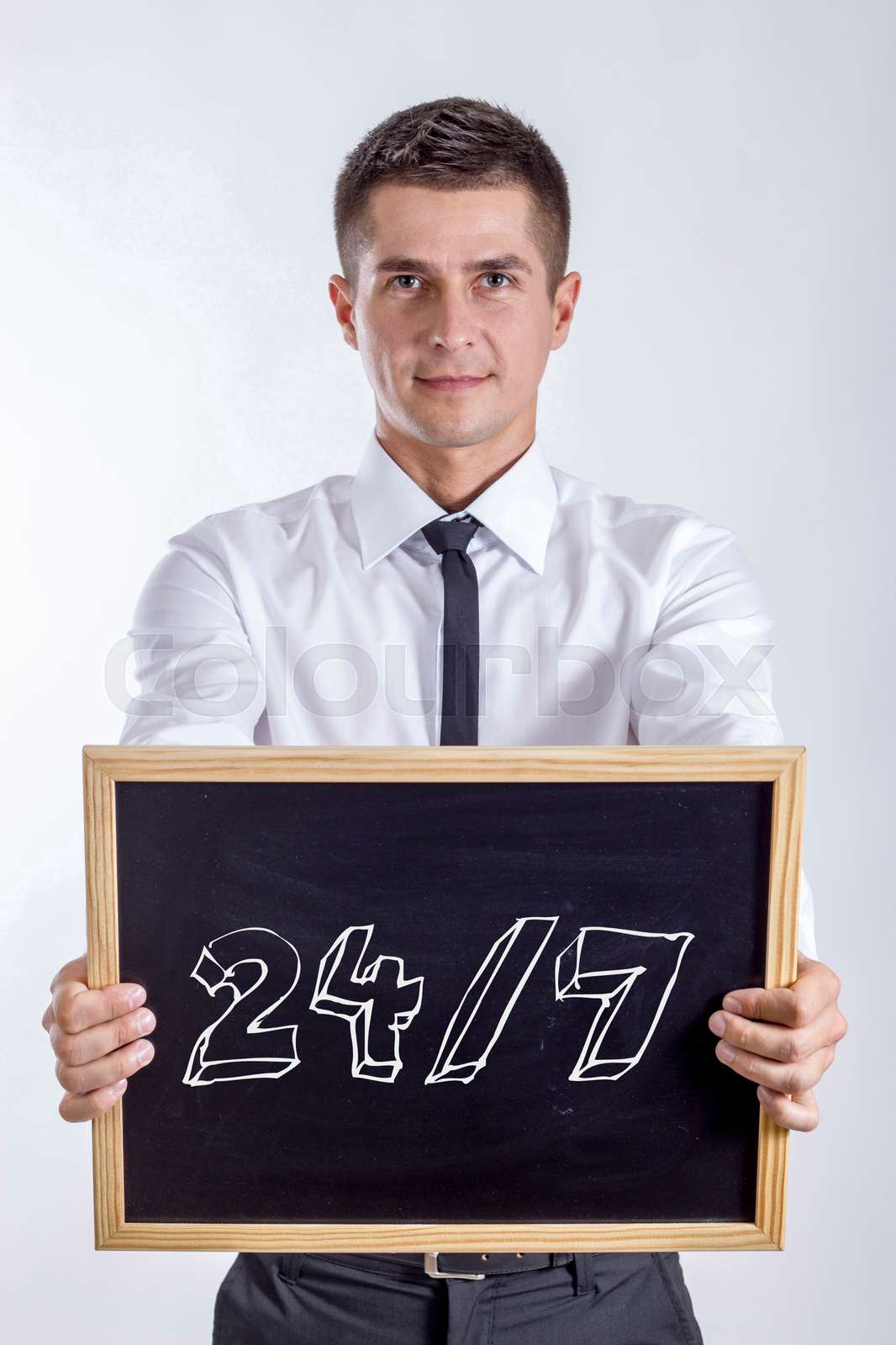 24 7 SERVICE Young businessman holding chalkboard with tex Colourbox