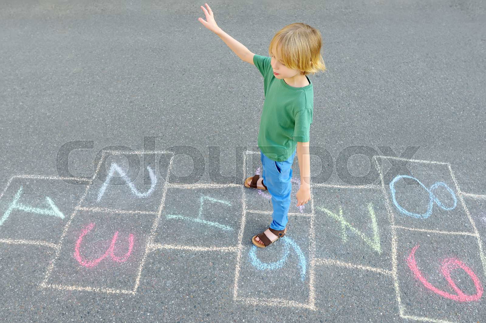 Little boy jumping by hopscotch drawn on asphalt. Child play Colourbox